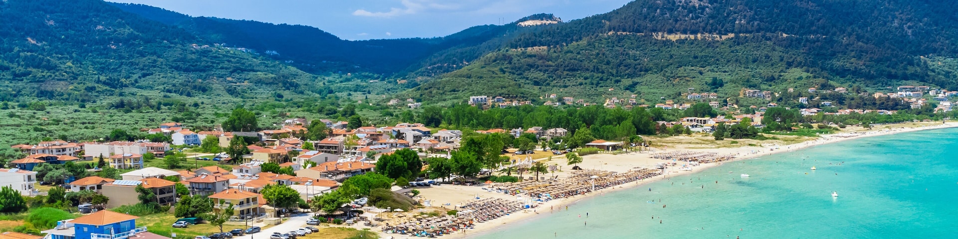 Uma vila costeira com praia, montanhas e edifícios residenciais.