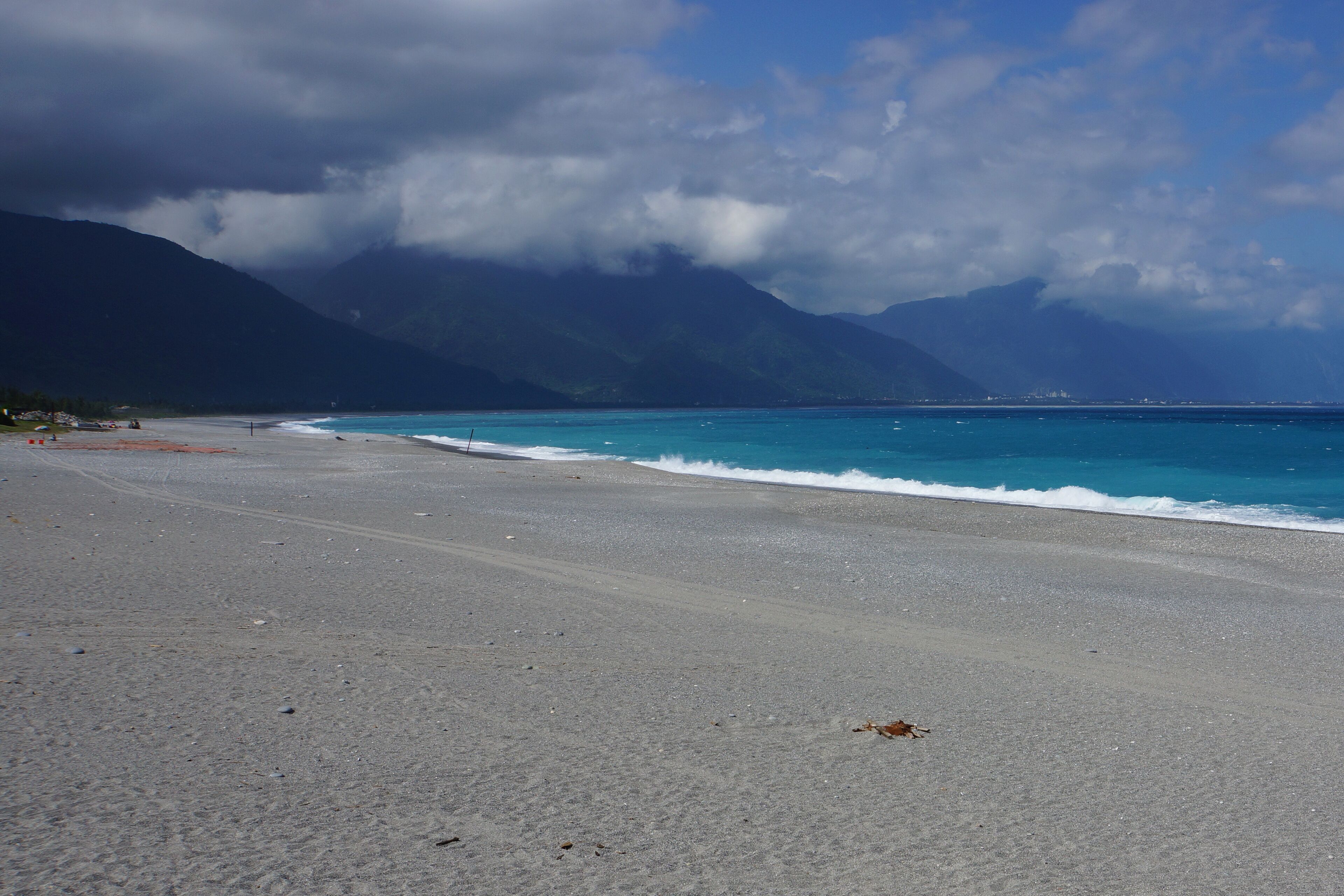 Uma praia com águas turquesa cristalinas, areia dourada e montanhas ao fundo.