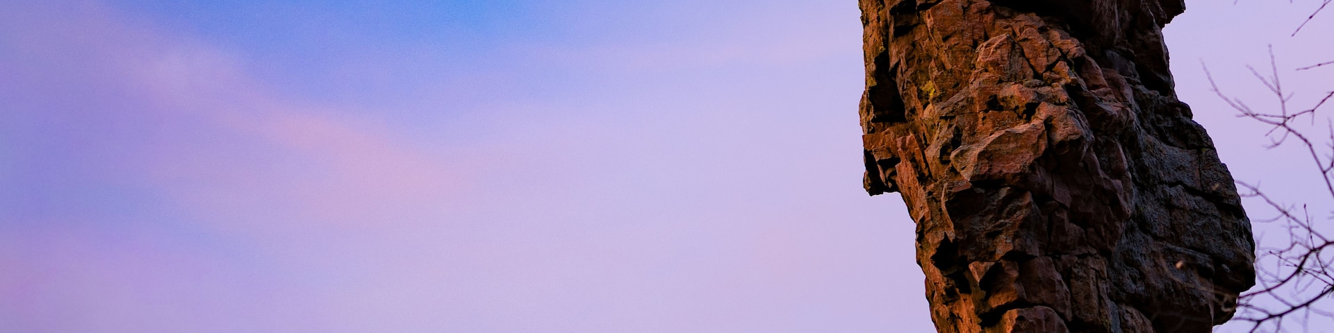 Formação rochosa imponente e acidentada contra um céu com tons suaves de rosa e azul.