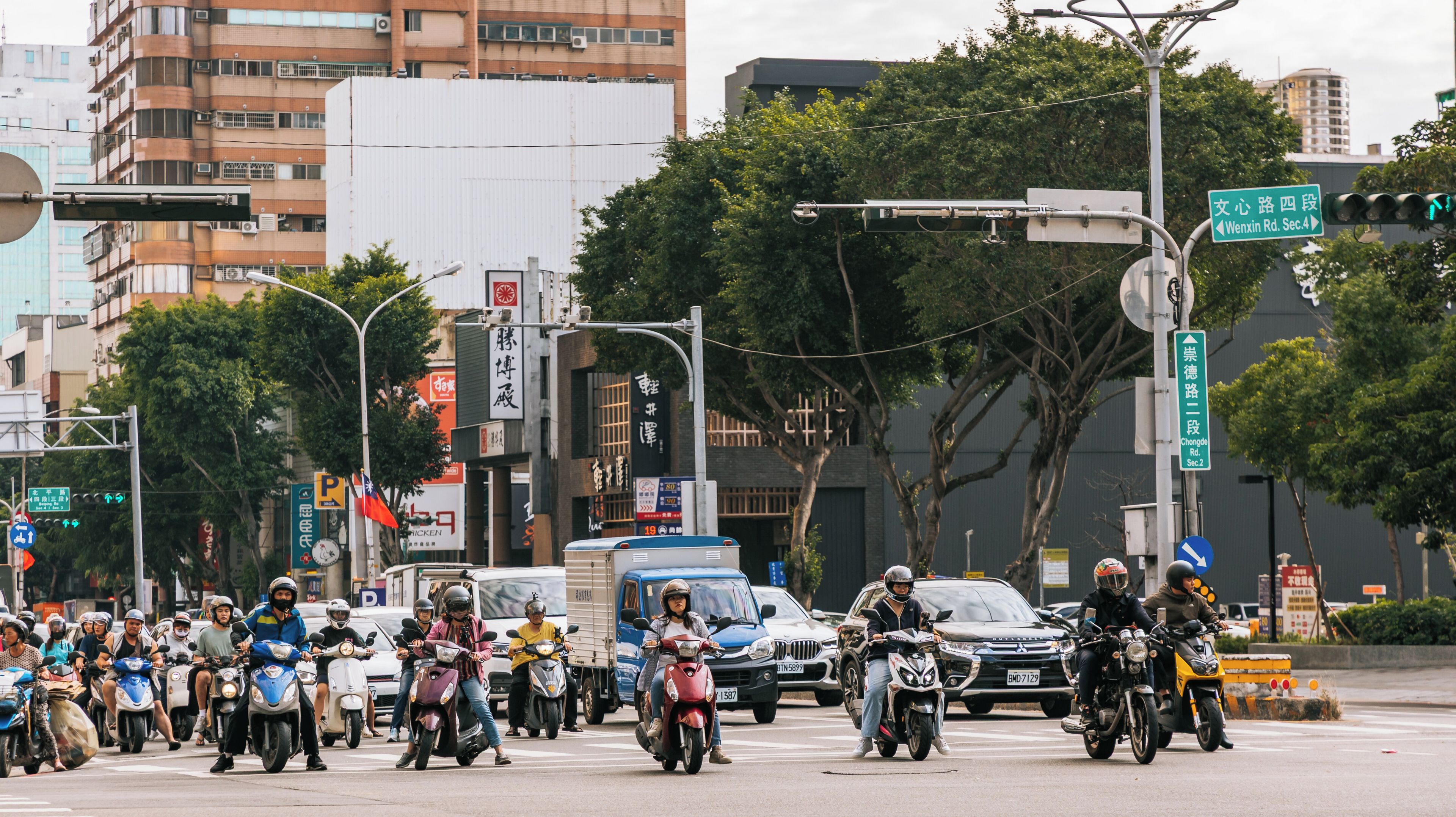 Uma rua urbana movimentada com vários motociclistas, carros e pedestres.