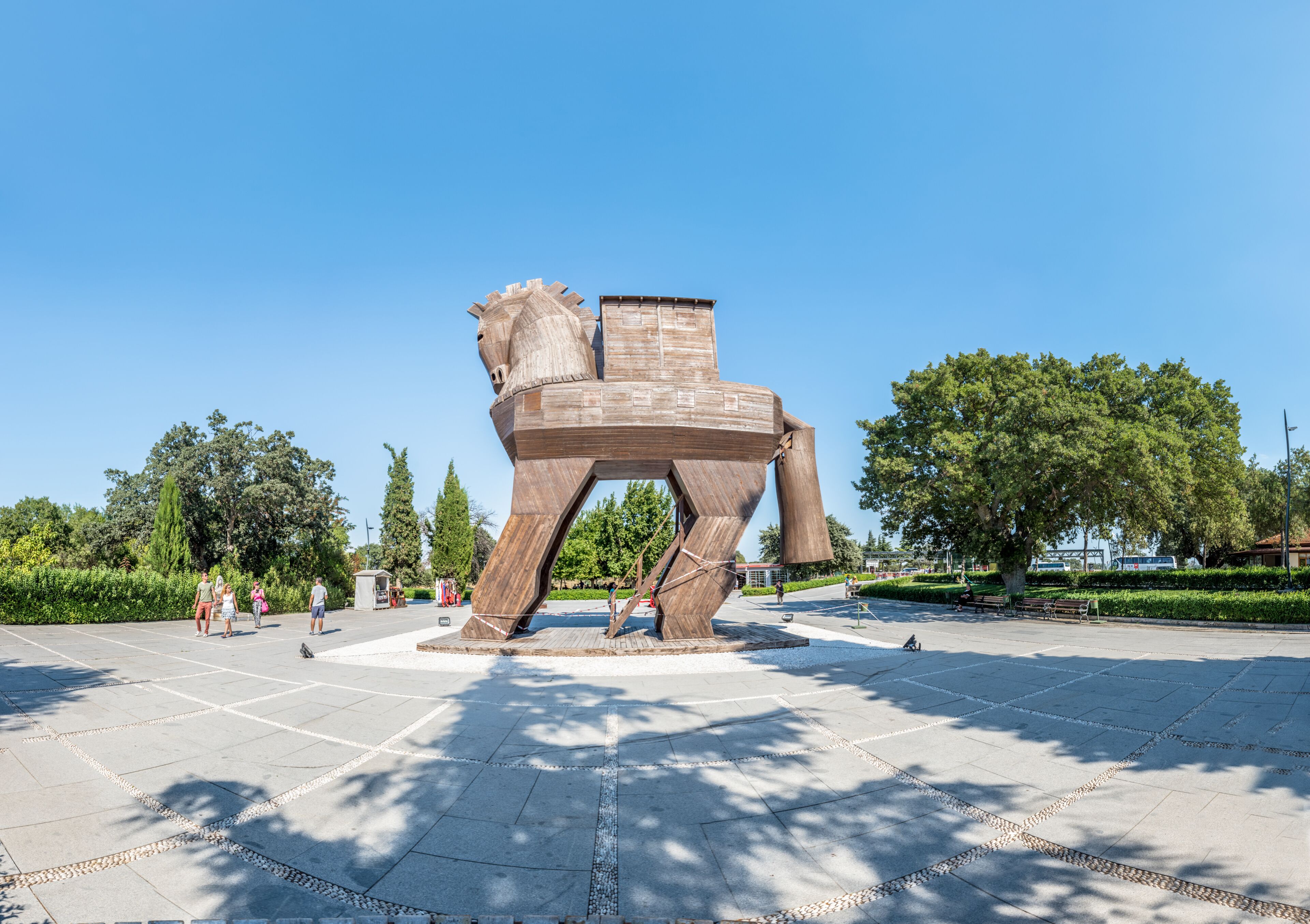 Uma grande estátua de bronze de um cavalo e seu cavaleiro em uma praça aberta, com árvores e céu claro.