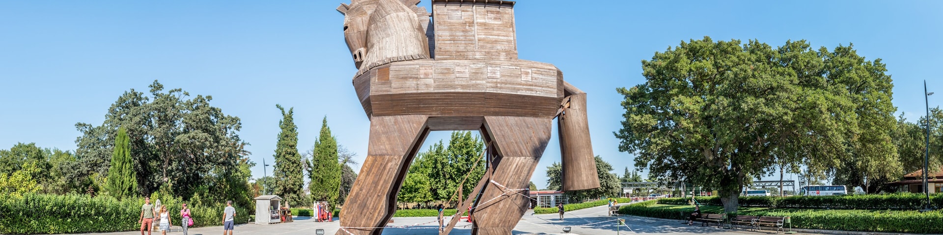 Uma grande estátua de bronze de um cavalo e seu cavaleiro em uma praça aberta, com árvores e céu claro.