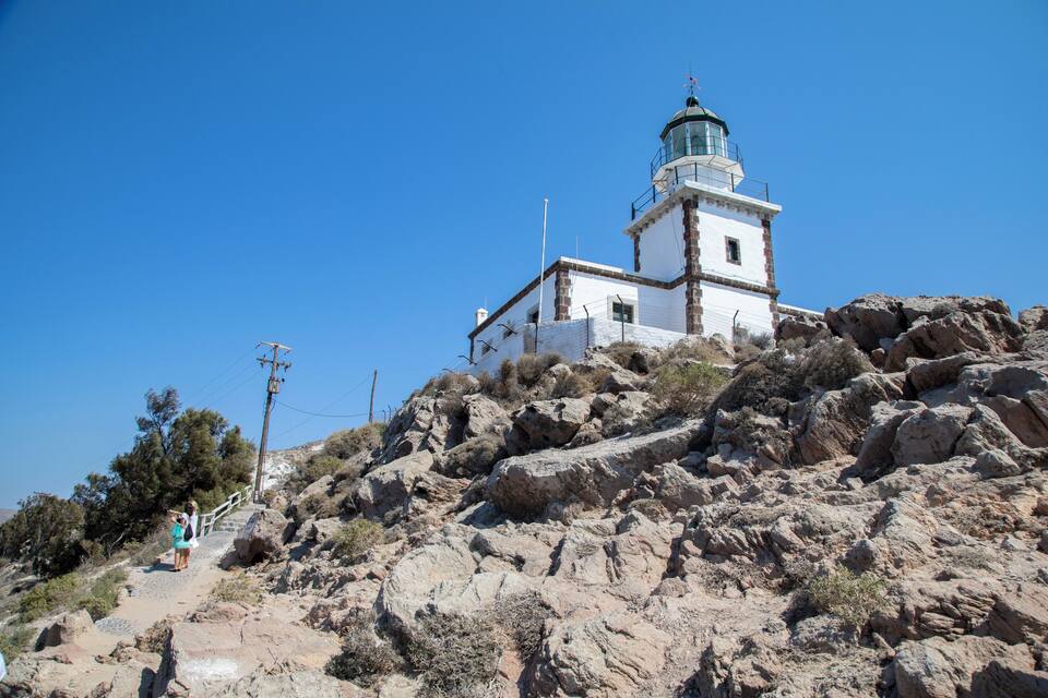 Um farol branco numa colina rochosa com um céu azul límpido.