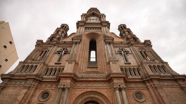 Uma igreja de pedra grande com uma porta em arco central, duas torres de sino e um relógio no topo.