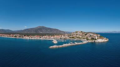 Uma cidade costeira com uma montanha ao fundo e um céu azul límpido.