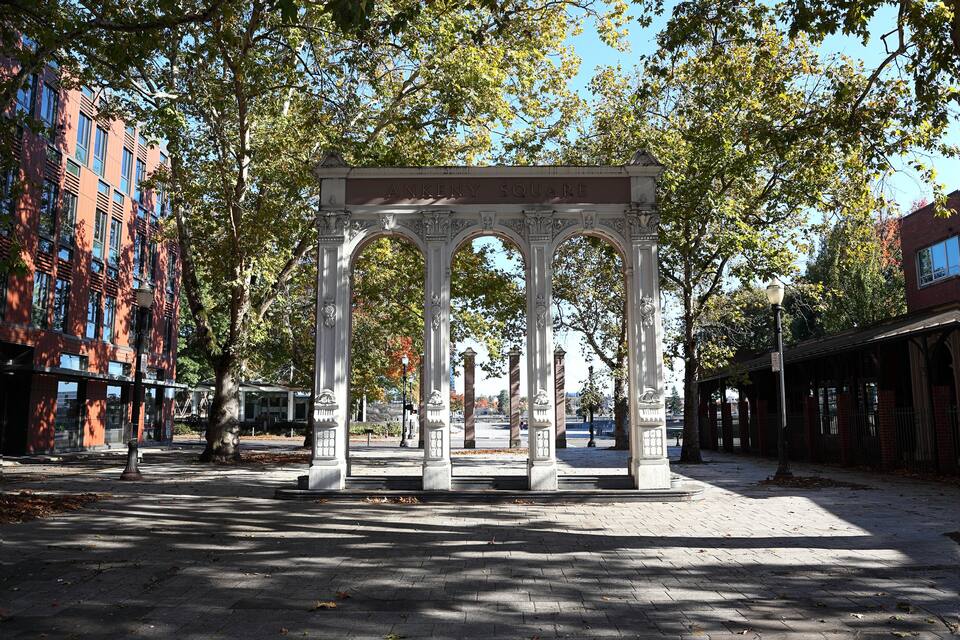 Um parque com um monumento central identificado como 'Ankeny Square', rodeado por árvores e edifícios.
