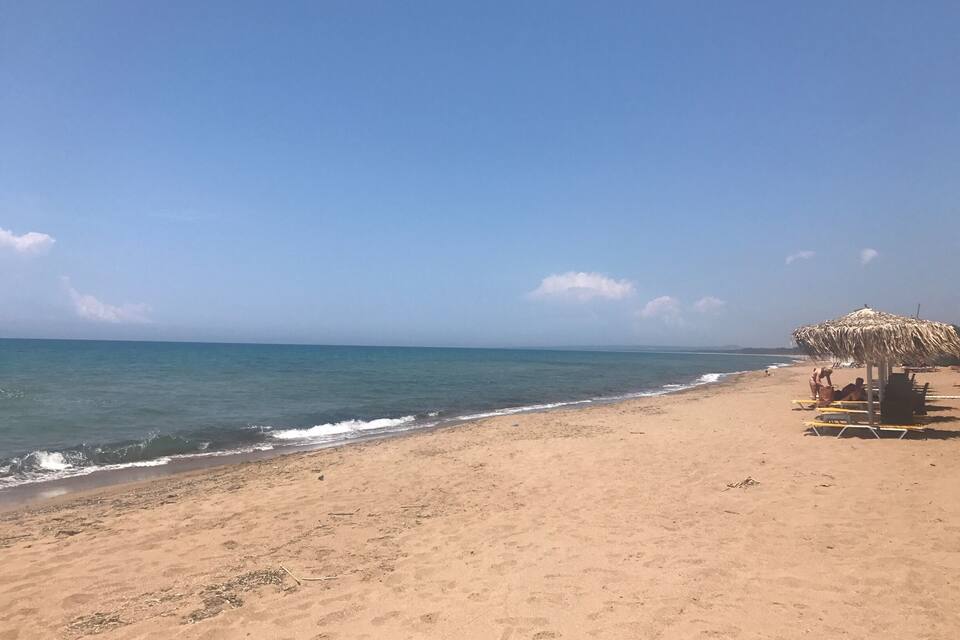 Uma praia arenosa com um guarda-sol de palha e espreguiçadeiras.