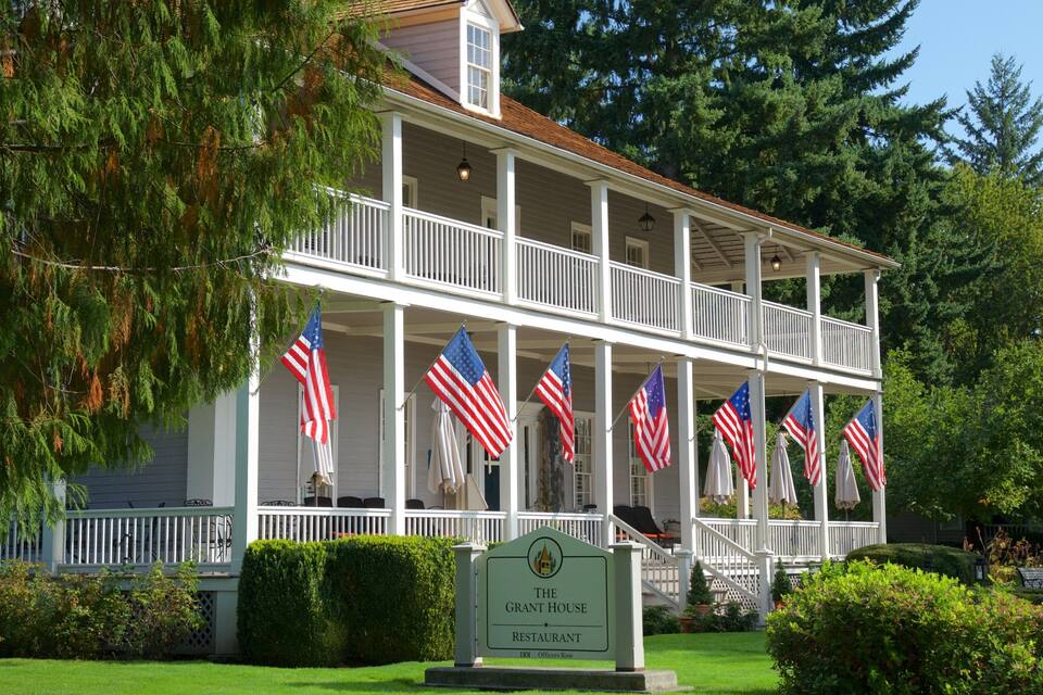 Um edifício de dois andares com varanda, várias bandeiras americanas e um letreiro que diz 'The Grant House Restaurant'.
