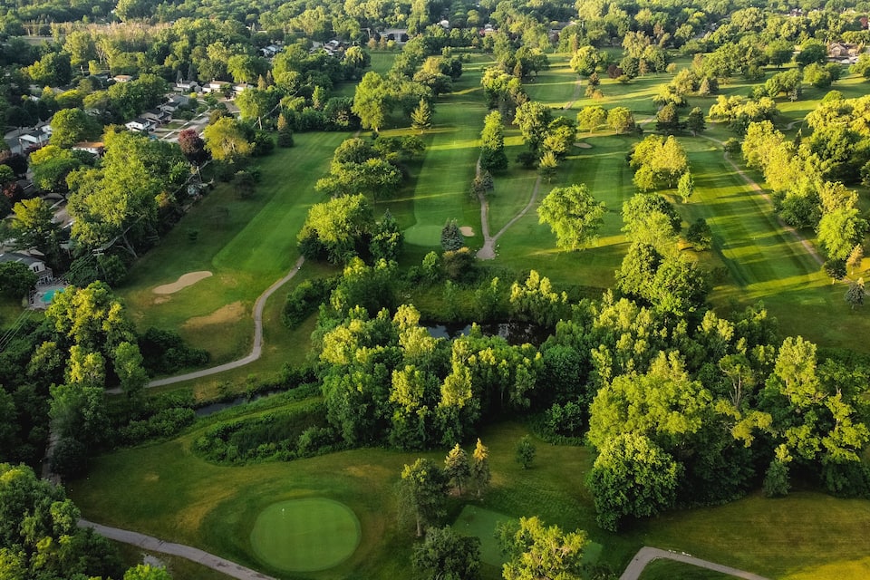 Vista aérea de um campo de golfe com vegetação exuberante, um lago e casas residenciais ao fundo.