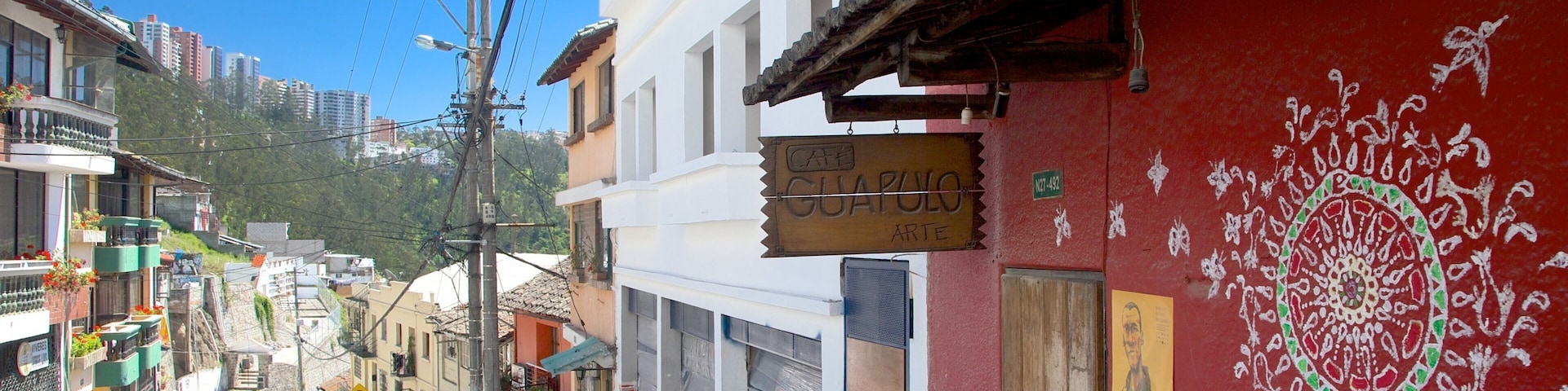 Rua estreita com edifícios, uma placa para 'Cafe Guapo Arte' e um mural numa parede vermelha.