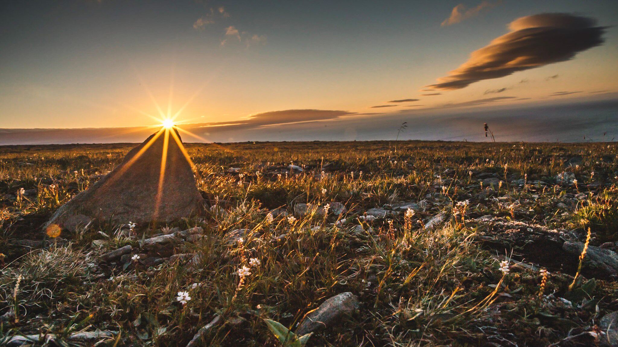 Um pôr do sol sobre um campo rochoso com vegetação escassa.