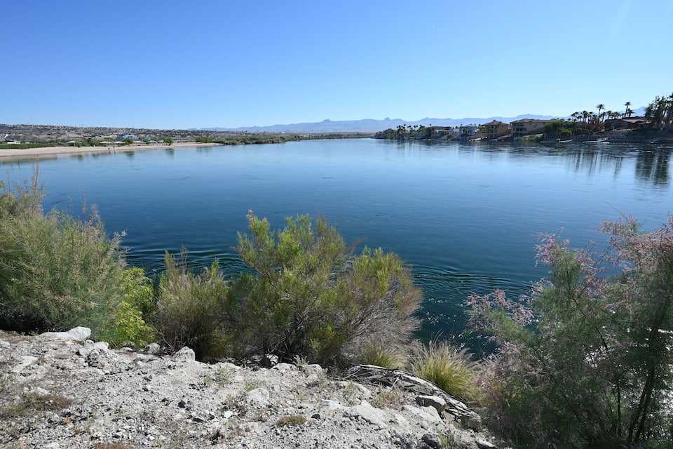 Um lago calmo com águas azuis e límpidas, rodeado por terreno rochoso e vegetação escassa.