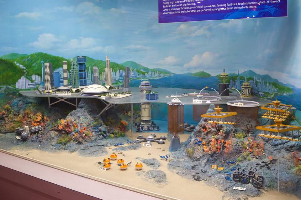 Um modelo detalhado de uma cidade costeira futurista, com infraestrutura avançada, incluindo uma ponte, diversos edifícios e recifes artificiais.