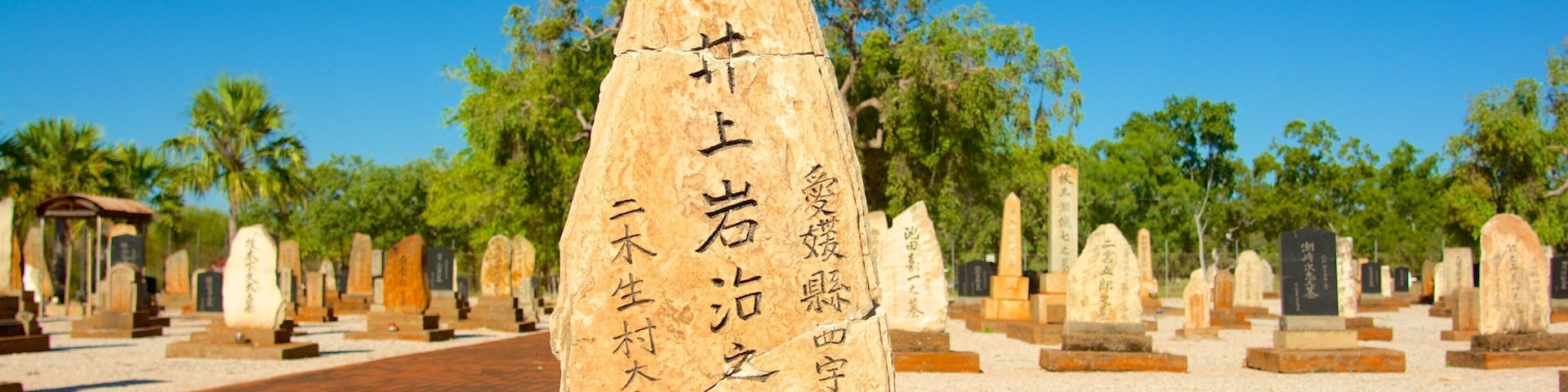 Um monumento de pedra com inscrições em um cemitério rodeado por árvores e outros túmulos.