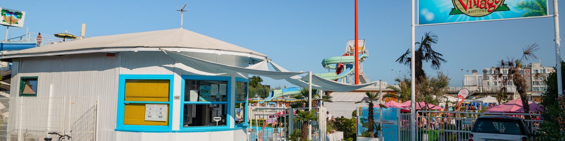 Um quiosque à beira-mar com esquema de cores azul e branco, um toboágua e uma placa para Beach Village Riccione.