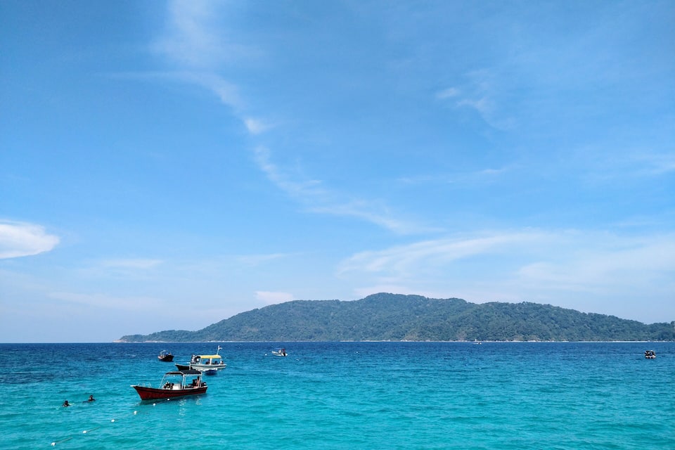 Um mar azul-turquesa com vários barcos, céu claro e uma ilha verde distante.
