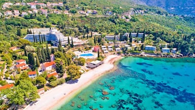 Vista aérea de uma área costeira com praia, águas turquesa cristalinas e um conjunto de edifícios, incluindo um hotel e moradias.