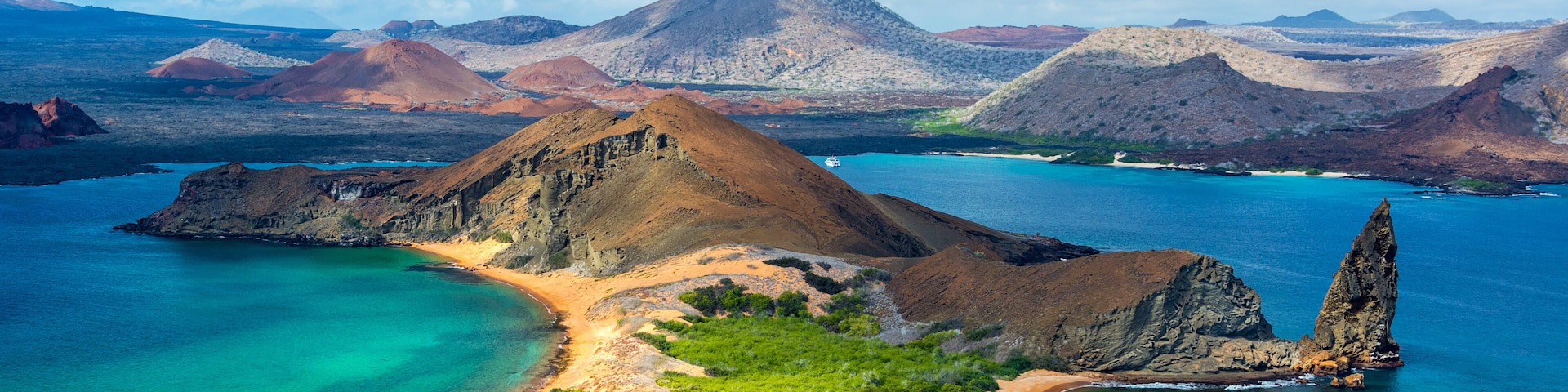 Paisagem costeira com uma montanha imponente, águas turquesa cristalinas e uma praia arenosa.