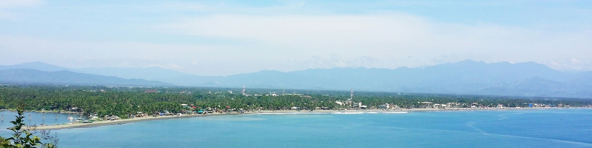 Paisagem costeira com mar azul cristalino, uma praia arenosa e uma cordilheira ao longe.