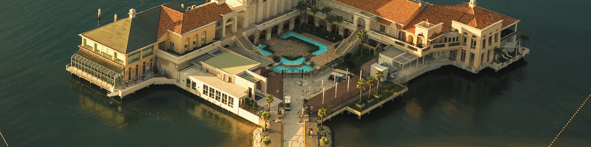 Vista aérea de uma propriedade costeira com uma grande piscina, uma praia e um píer.