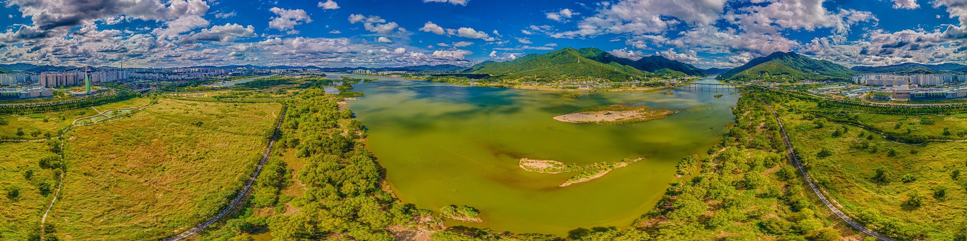 Um rio cercado por colinas verdes, uma ponte e uma paisagem urbana ao longe.