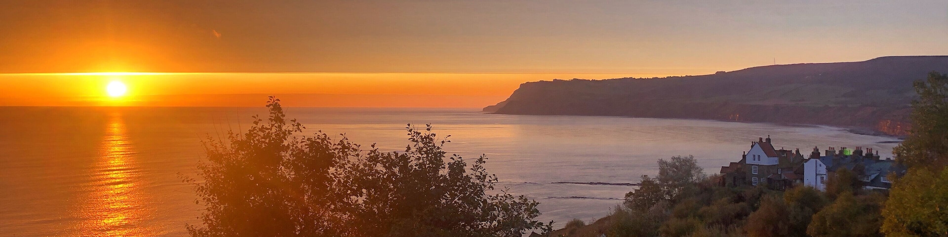 Um pôr do sol sobre uma paisagem costeira, com um caminho que leva a um conjunto de casas.