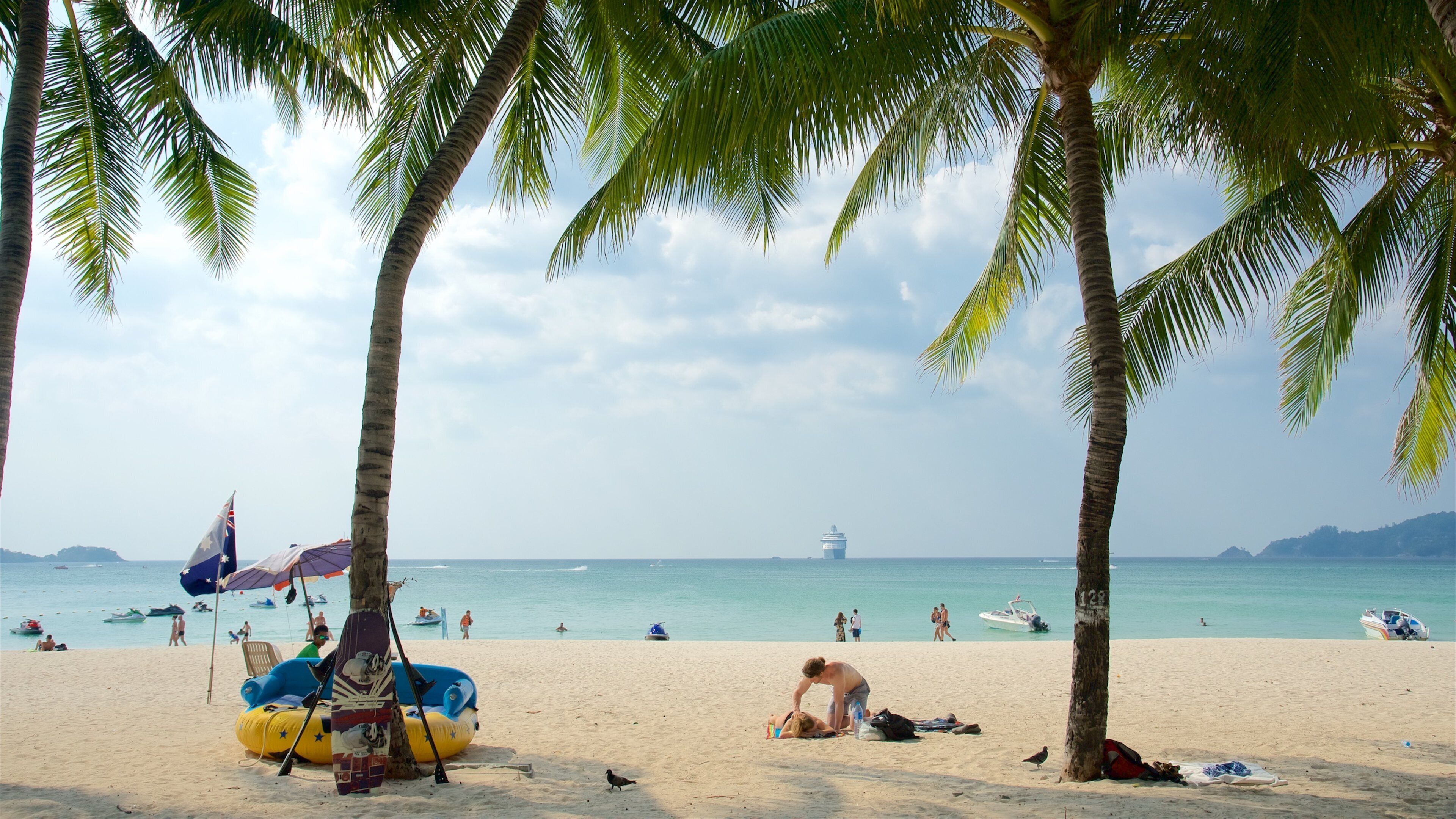 Uma praia com palmeiras, boias infláveis e um navio ao longe.