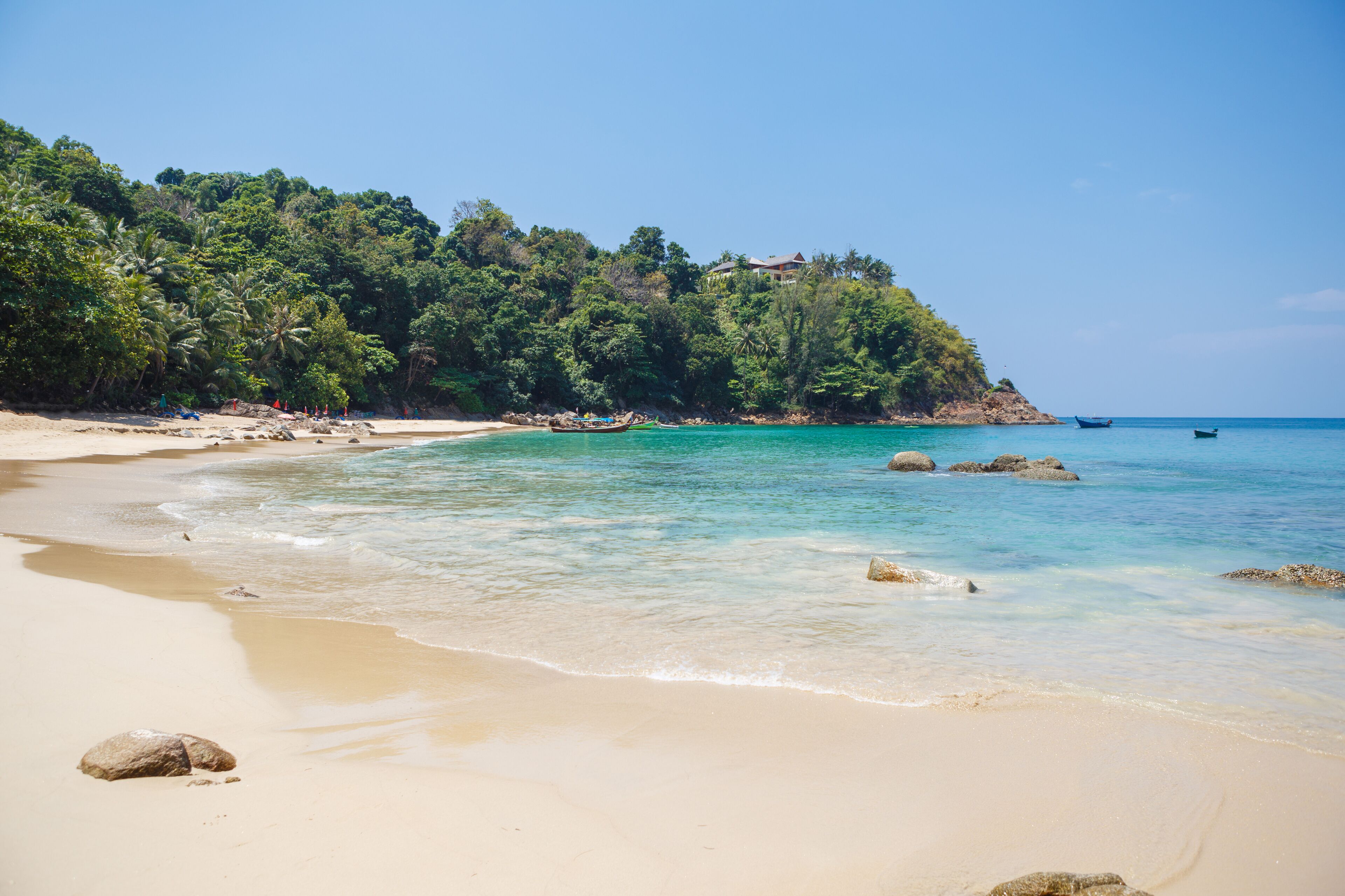 Uma praia com águas turquesa cristalinas, areal arenoso e uma colina arborizada ao fundo.