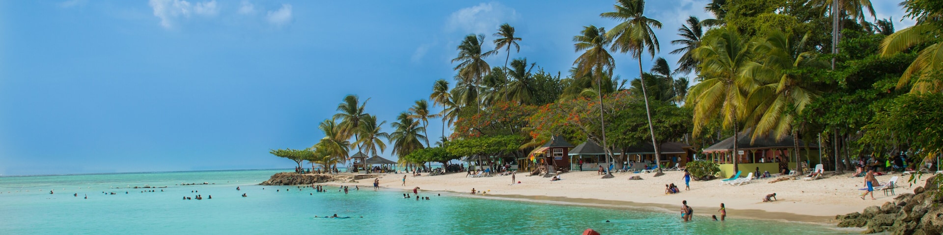 Uma praia tropical com águas turquesa cristalinas, um barco salva-vidas amarelo e palmeiras.