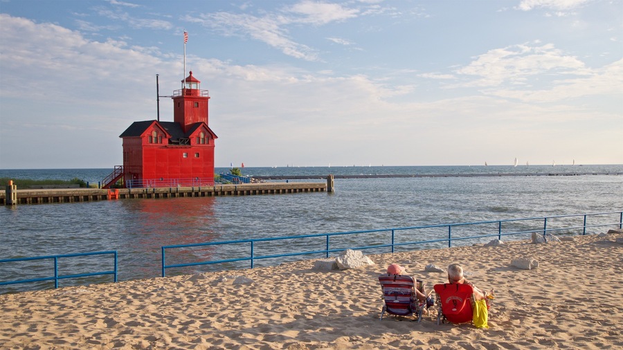 Um farol vermelho sobre um cais, uma praia arenosa e duas pessoas sentadas em cadeiras de praia.