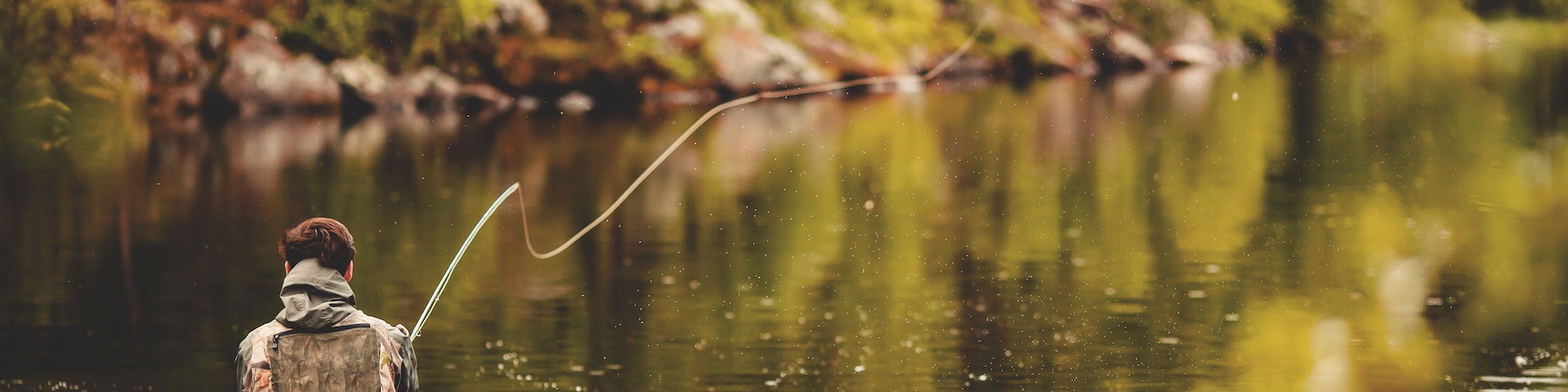 Uma pessoa pescando em um rio calmo, cercada por vegetação densa.