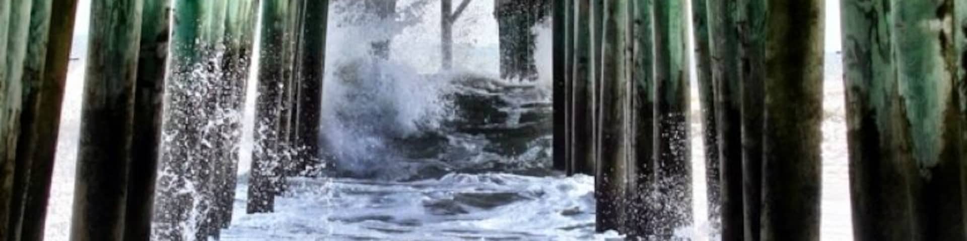 Um píer de madeira com ondas quebrando por baixo.