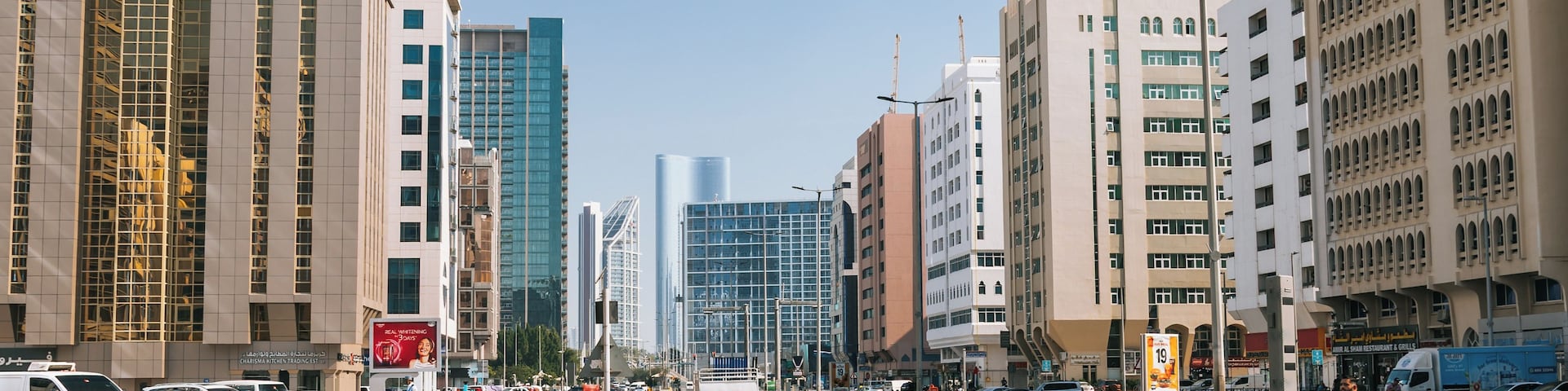 Rua urbana com edifícios modernos, um ciclista e uma faixa de pedestres.