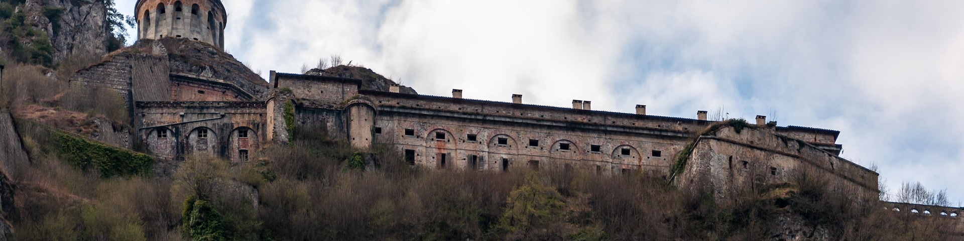 Um edifício grande e histórico com cúpula e janelas em arco, rodeado por terreno rochoso e vegetação escassa.