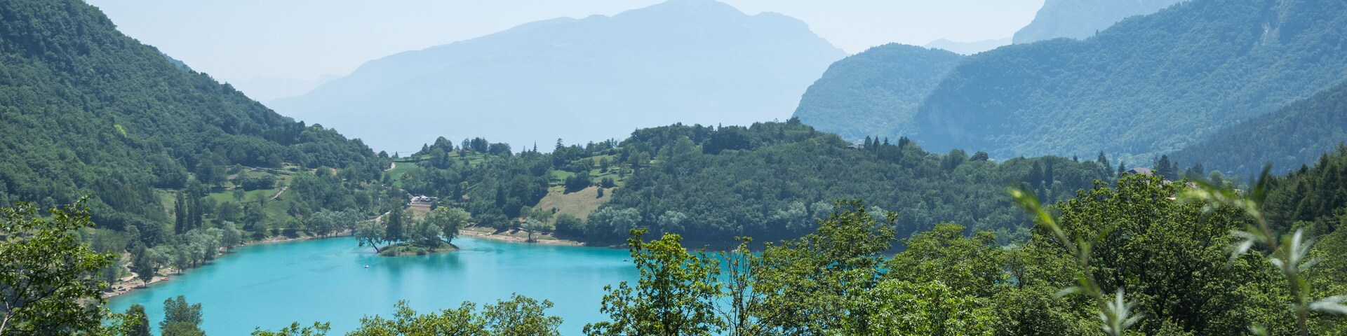 Um lago azul-turquesa rodeado por montanhas verdes e florestas densas.