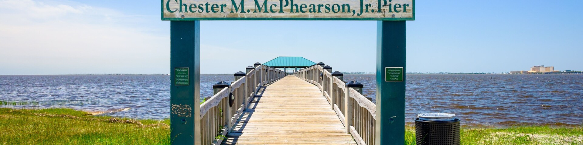 Um cais que leva ao Pier Chester M. McPhearson Jr., com vista para a água e edifícios ao longe.