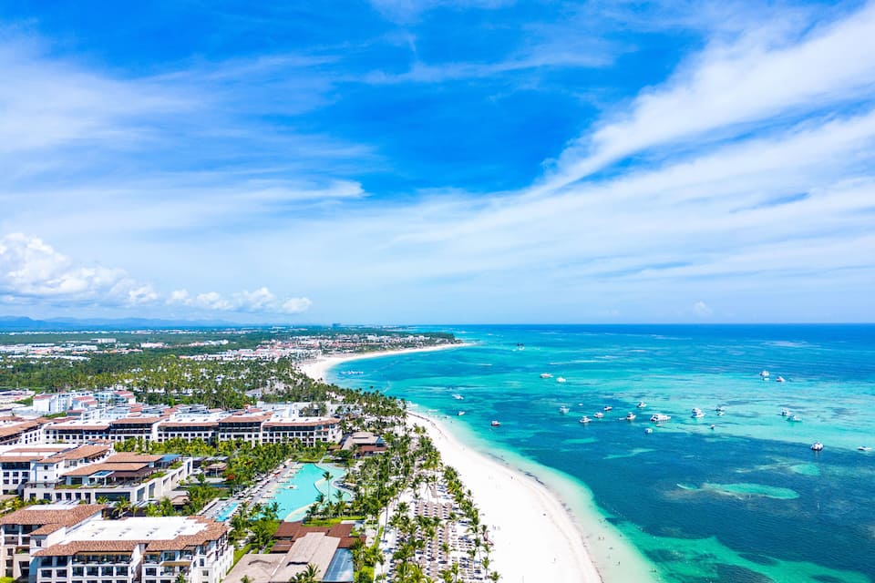 Uma área de resort costeira com uma praia, águas turquesa cristalinas e céu claro.
