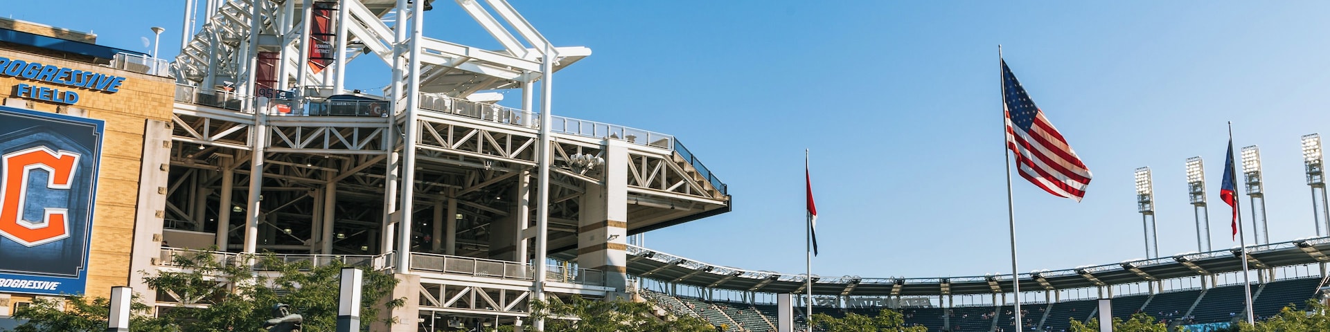 Estádio de beisebol com um grande logotipo em formato de 'C', bandeiras americanas e uma multidão de pessoas.