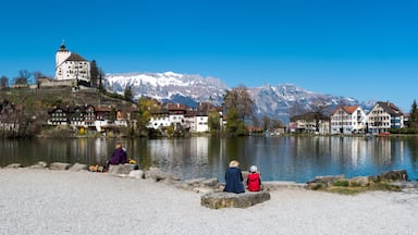 Um lago com casas e um castelo numa colina, rodeado por montanhas.