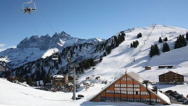 Um teleférico de esqui, montanhas cobertas de neve, um edifício de estação de esqui e um céu azul claro.