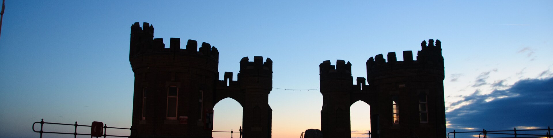 Silhueta de um castelo com duas torres e um arco central contra um céu crepuscular.