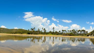 Uma praia com águas azul-claras, areal arenoso, uma rocha na água e uma montanha ao fundo.
