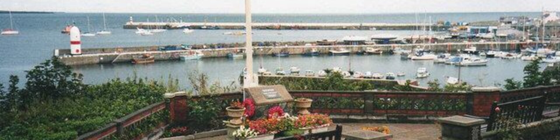 Um porto com barcos, um farol e um mastro.