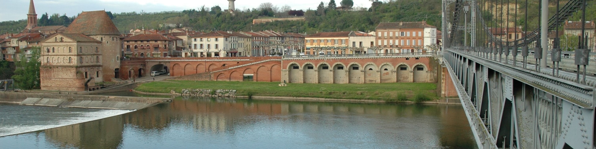 Uma ponte sobre um rio calmo, com edifícios históricos e uma torre ao fundo.