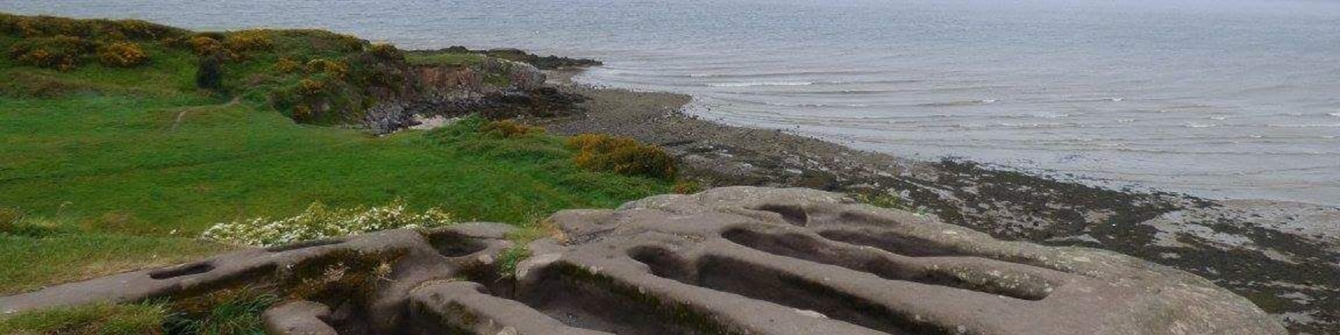Paisagem costeira com uma grande estrutura de pedra perto da praia.