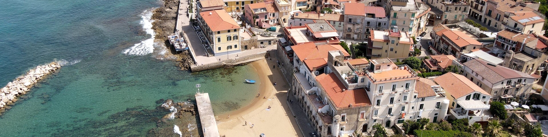 Uma vila costeira com praia, costa rochosa e edifícios em terraços.