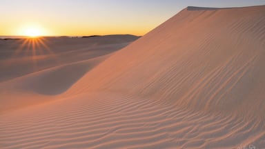 Dunas de areia com o sol se pondo ao fundo.