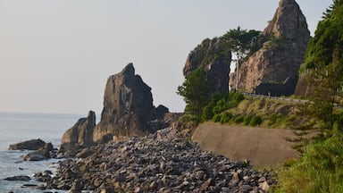 Litoral rochoso com formações rochosas marcantes e uma barreira de concreto.