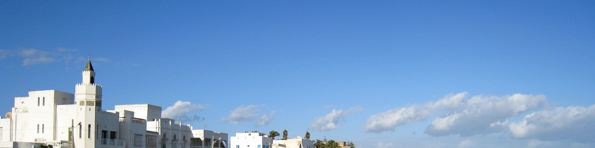 Uma vila costeira com edifícios brancos, uma linha costeira rochosa e um céu azul claro.