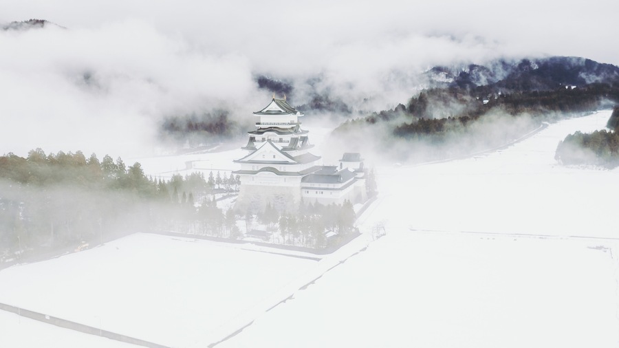 Um castelo japonês tradicional rodeado por uma paisagem nevada e montanhas.